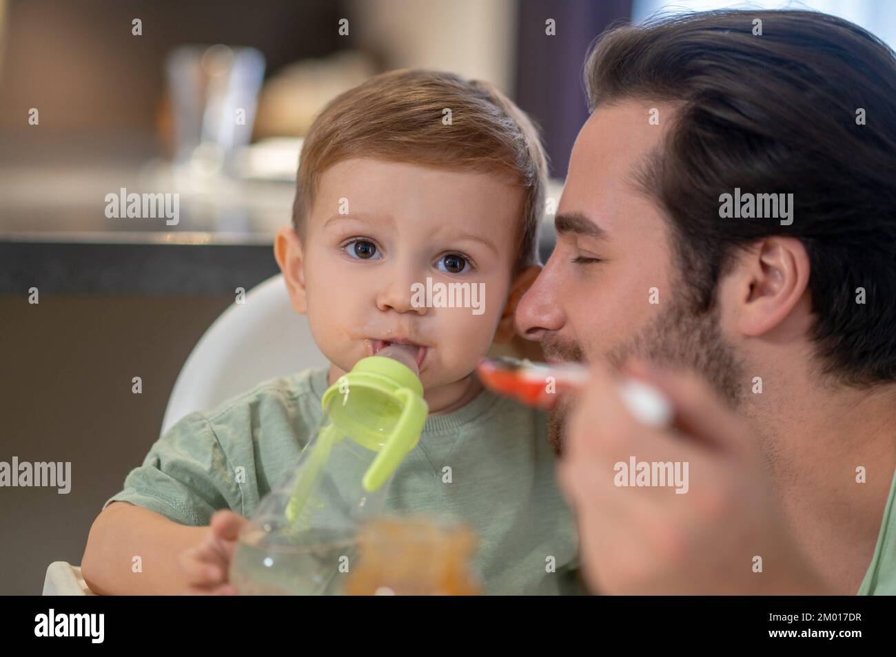 Eating. Cute little boy drinking from his bottle while dad feeding him ...