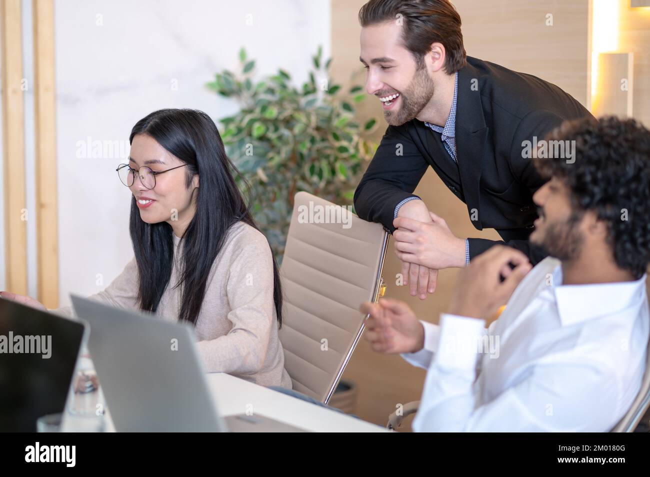 Joyous female employee seated at the office table pointing at something ...