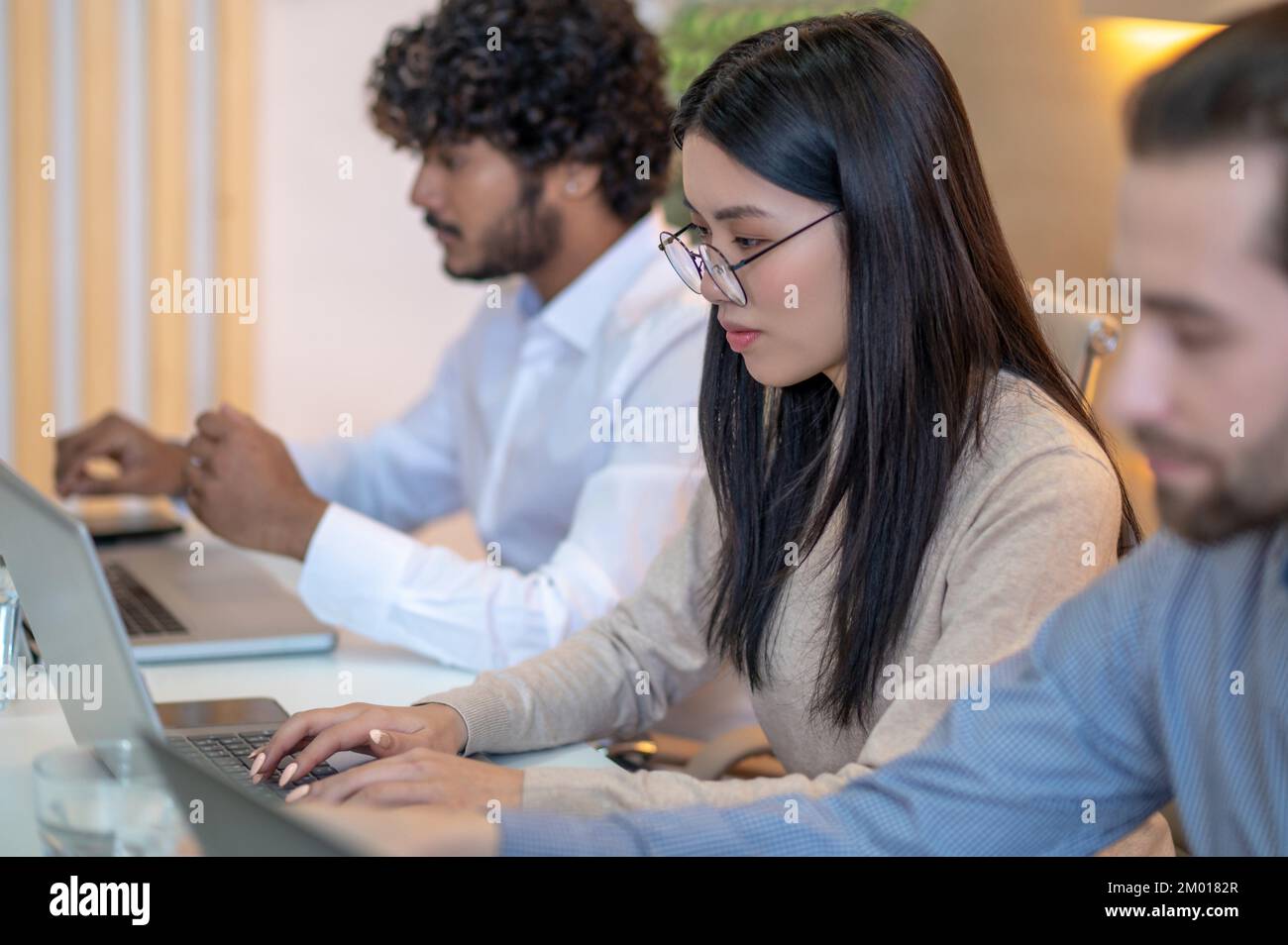 Concentrated female employee and her male colleagues seated at the ...