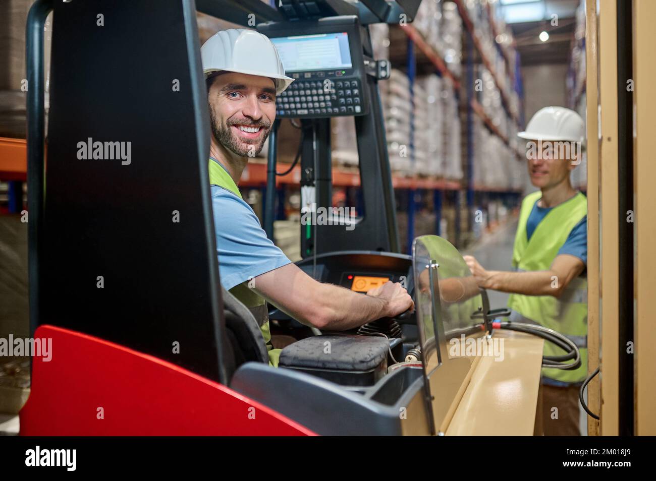 Cheerful lift truck operator and a warehouse loader standing among the ...