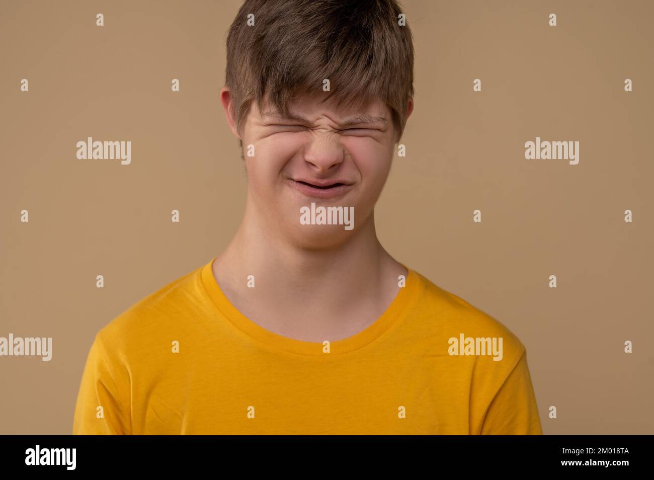 Portrait of a teenage boy standing against the wall and pulling a face ...
