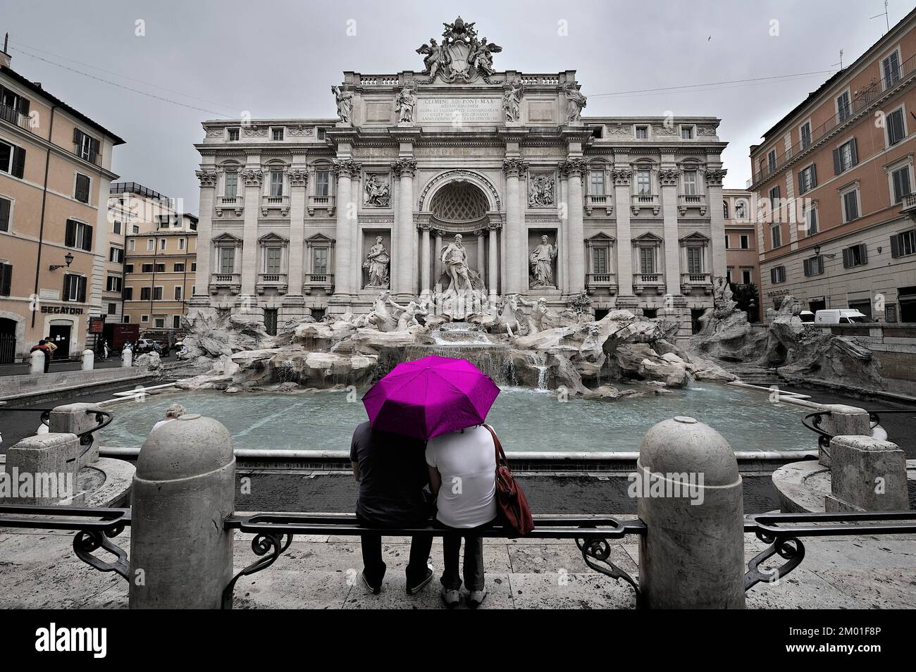 Image with low color saturation of a couple sitting in front of the Trevi Fountain on a hot pink ...