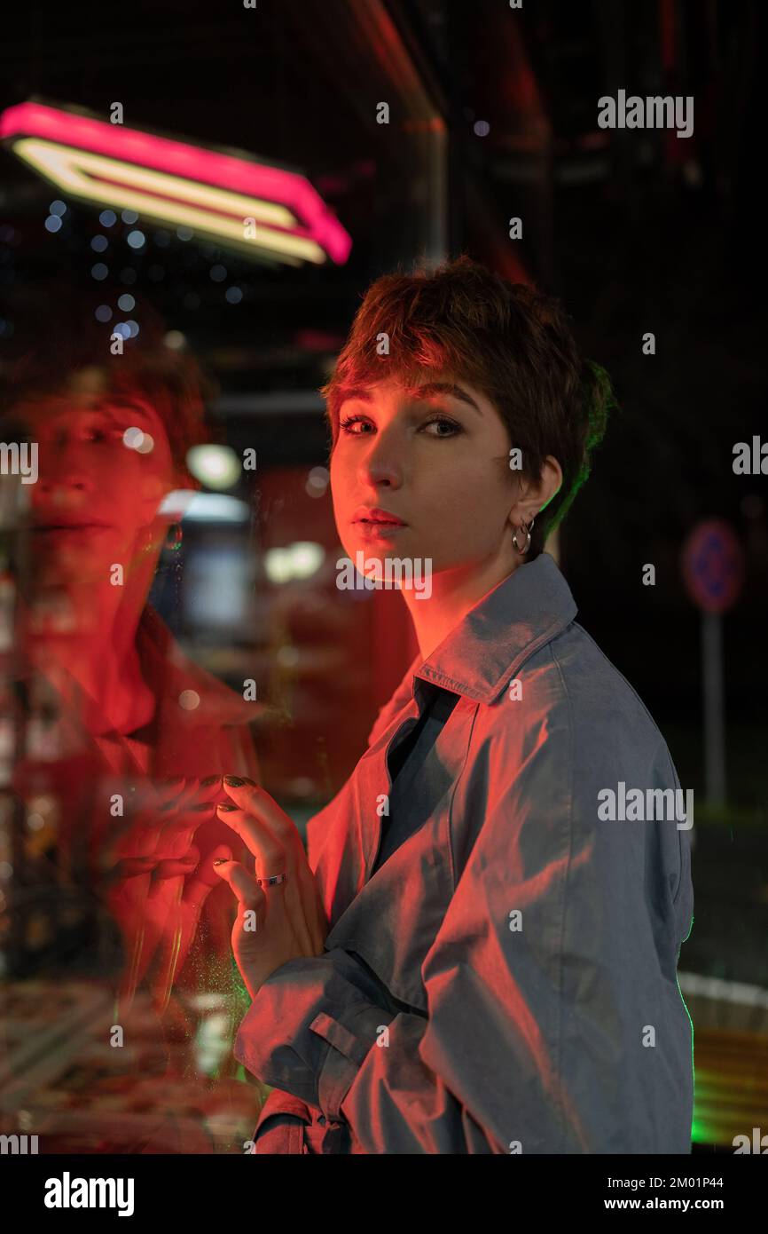 Sad lonely woman in red neon light leaning on shop window on street at ...