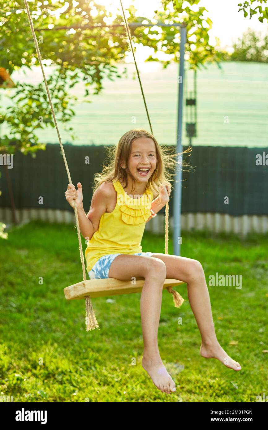 Happy barefoot laughing child girl swinging on a swing in sunset summer day on the backyard at ...