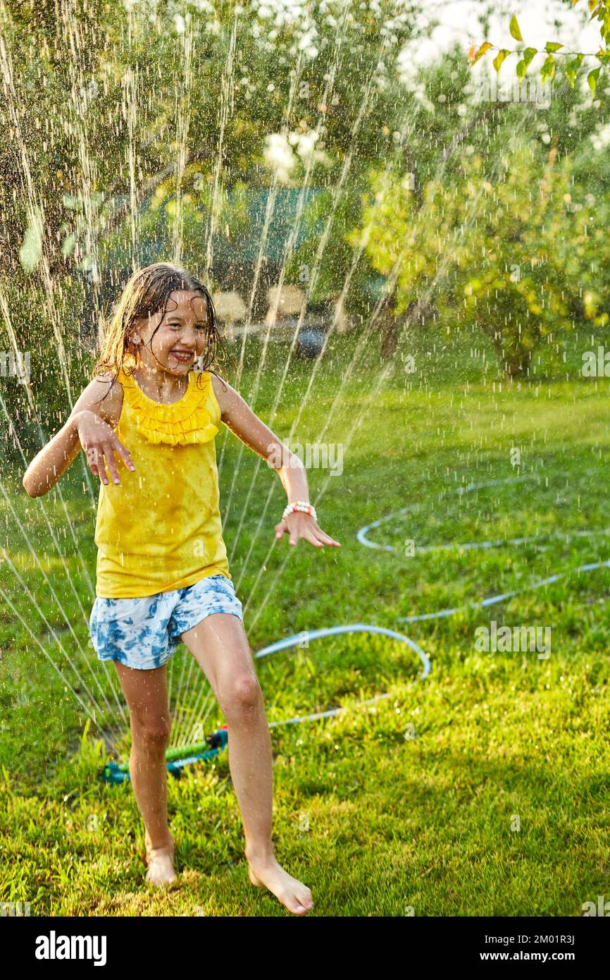 Happy kid girl playing with garden sprinkler run and jump, summer ...