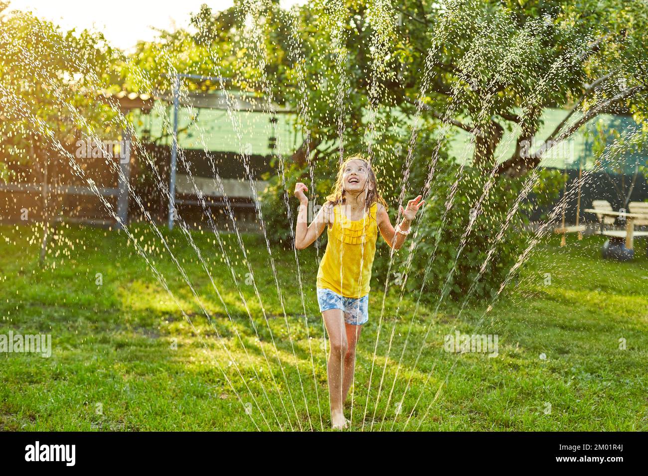 Happy kid girl playing with garden sprinkler run and jump, summer ...