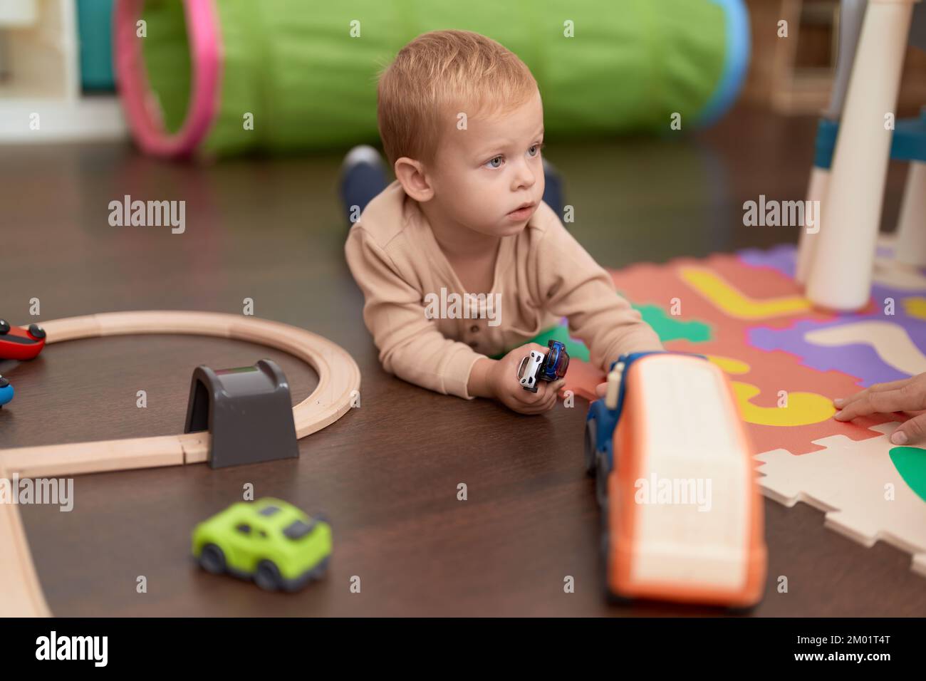 Adorable toddler playing with car toy lying on floor at kindergarten ...