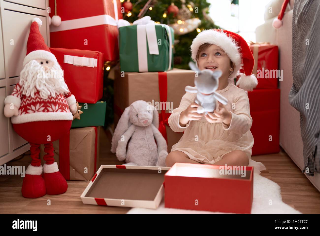 Adorable girl unpacking gift sitting by christmas tree at home Stock ...