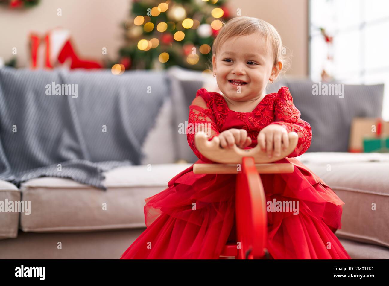 Adorable hispanic girl playing with reindeer rocking by christmas tree ...