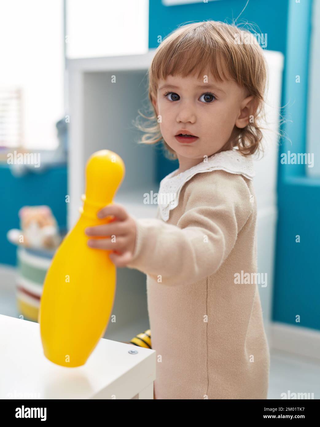 Adorable hispanic girl holding bowling pin standing at kindergarten ...