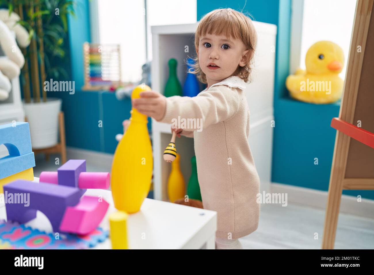 Adorable hispanic girl holding bowling pin standing at kindergarten ...