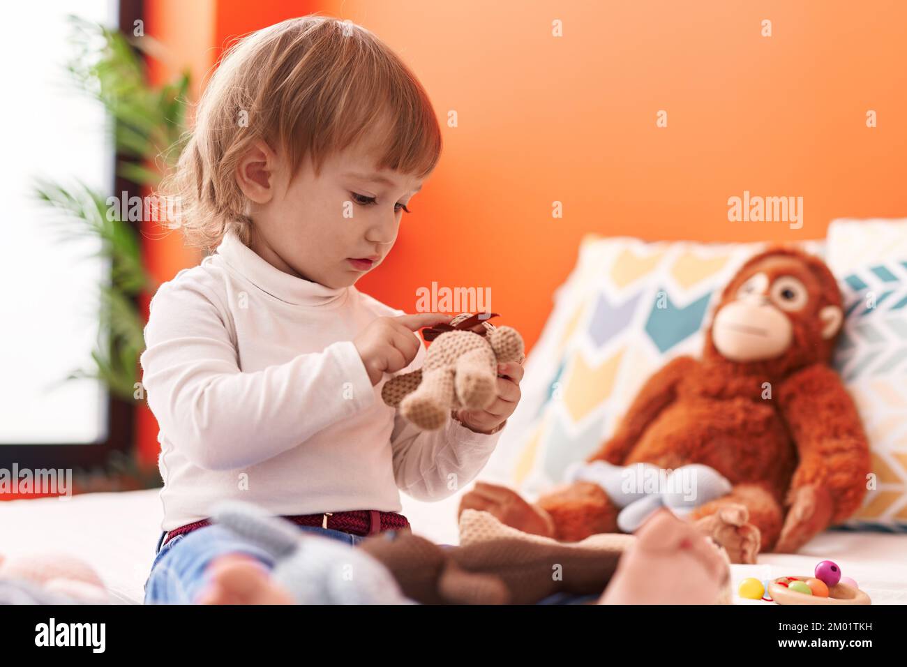 Adorable hispanic girl holding dolls sitting on bed at bedroom Stock ...