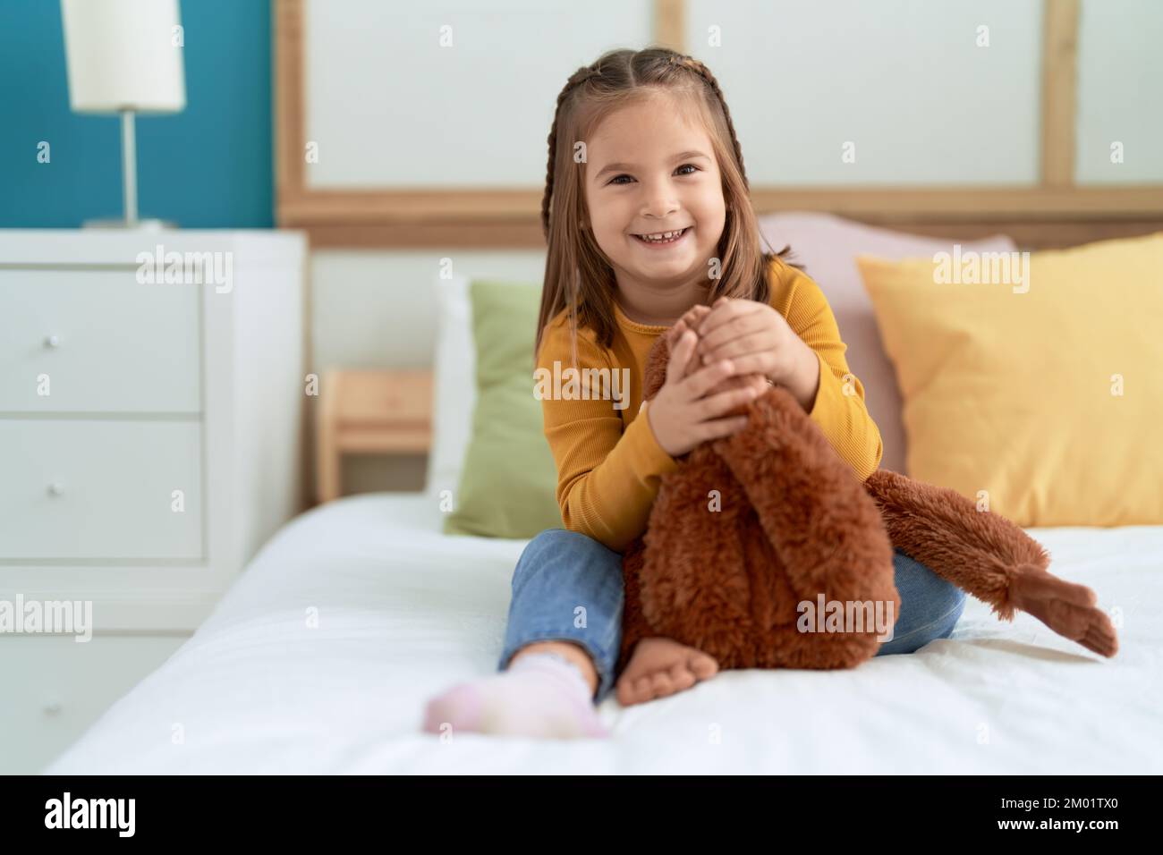 Adorable hispanic girl hugging monkey doll sitting on bed at bedroom ...