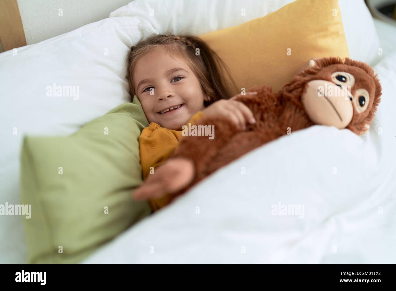 Adorable hispanic girl hugging monkey doll lying on bed at bedroom ...