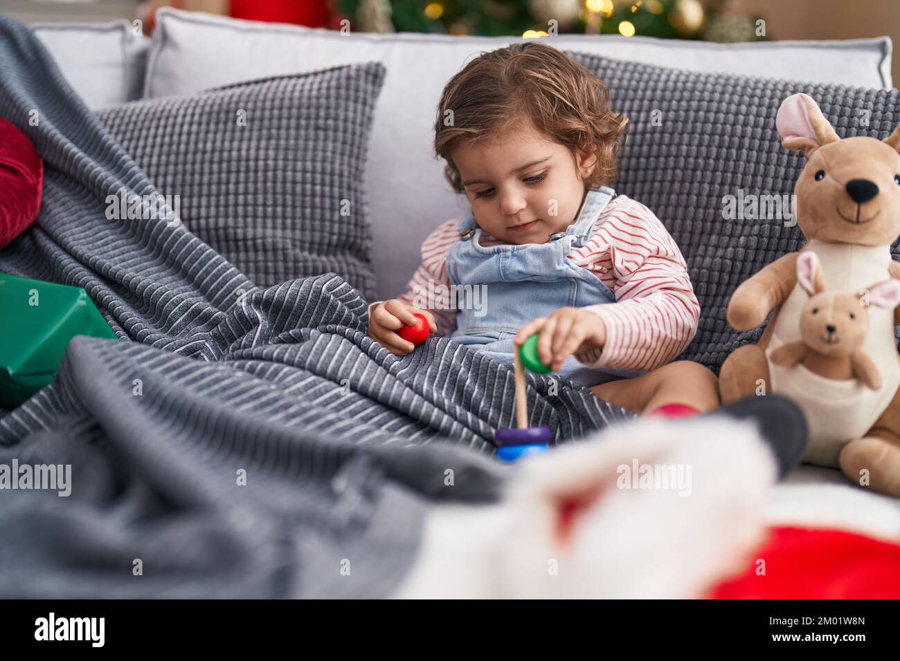 Adorable hispanic girl playing with hoops game sitting on sofa by ...