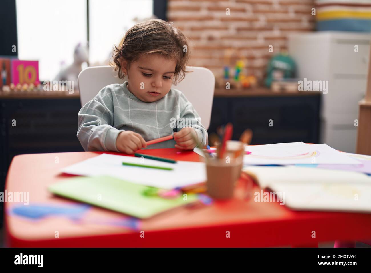 Adorable hispanic girl student sitting on table drawing on paper at ...