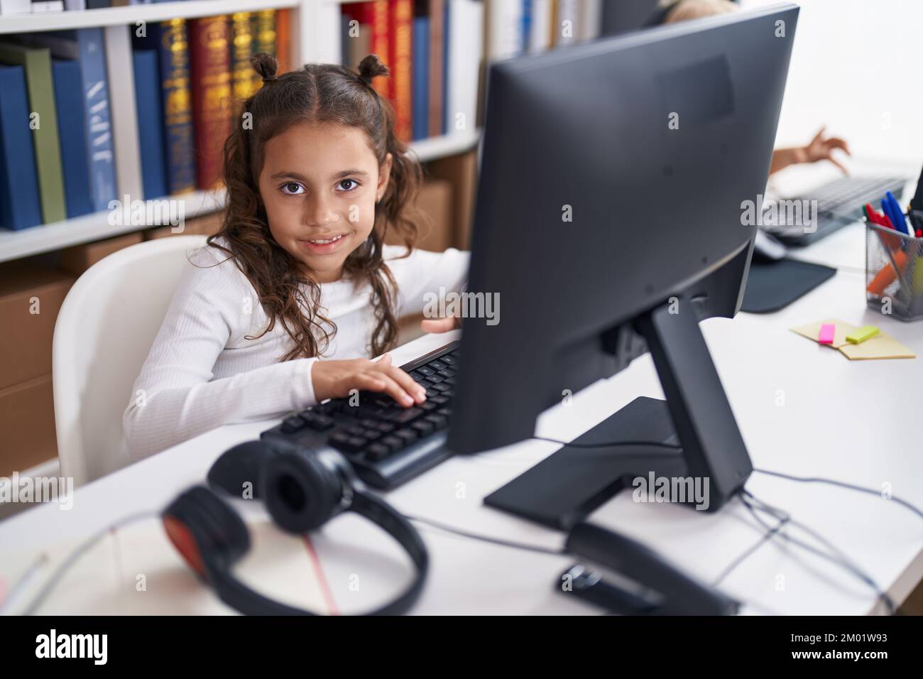 Adorable hispanic girl student using computer sitting on table at ...