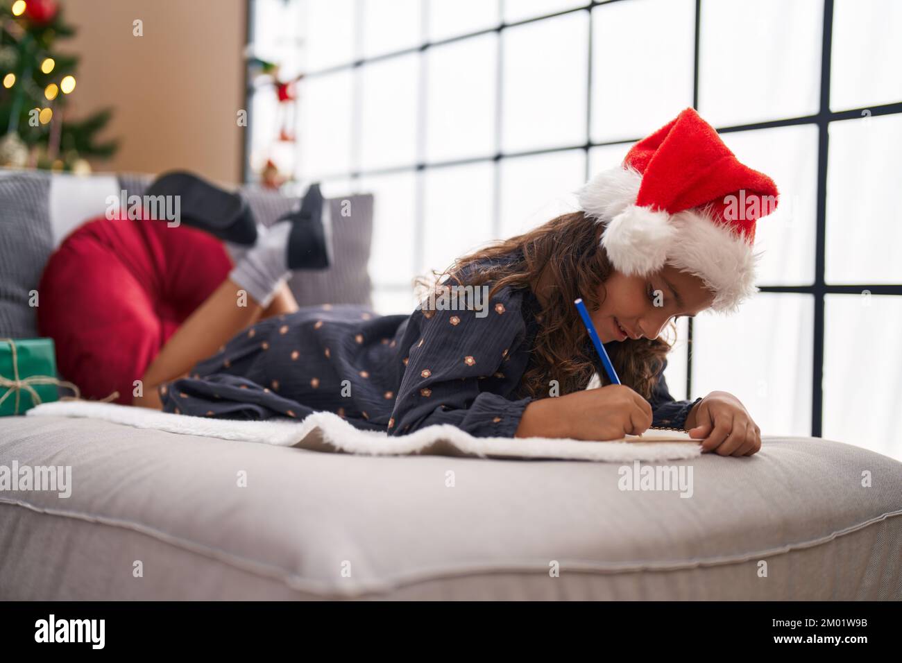 Adorable hispanic girl drawing on notebook lying on sofa by christmas ...