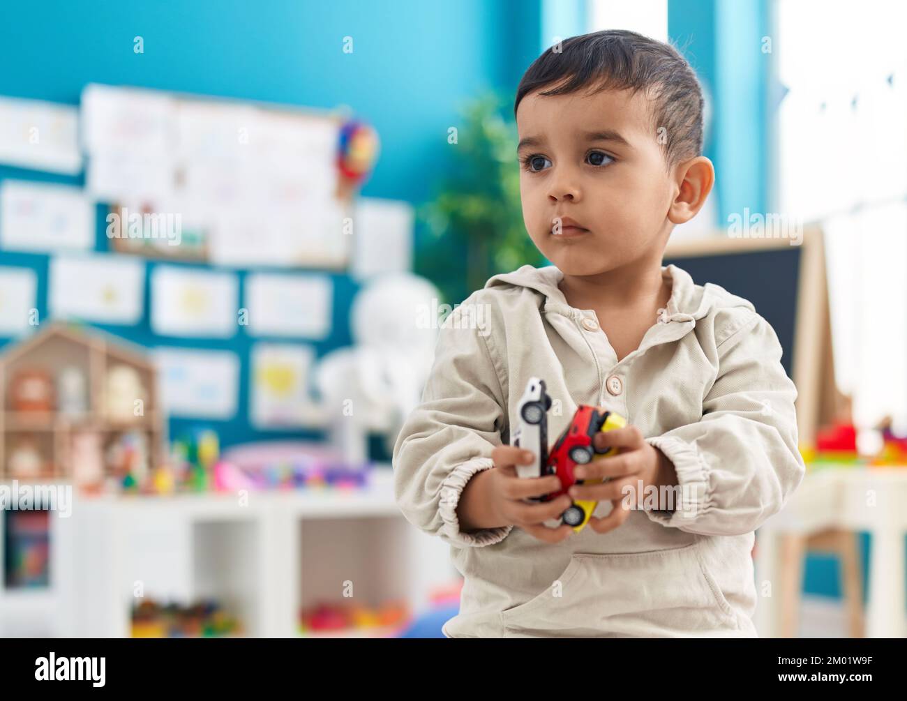 Adorable hispanic toddler holding car toy standing at kindergarten ...
