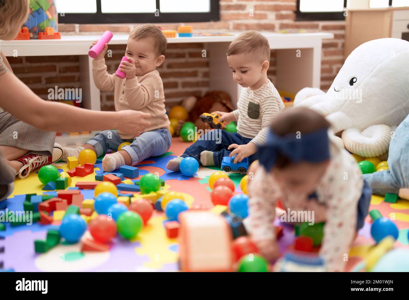 Group of toddlers playing with toys sitting on floor at kindergarten ...