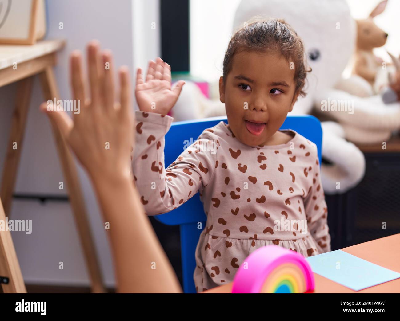 Adorable hispanic girl high five sitting on table at kindergarten Stock ...
