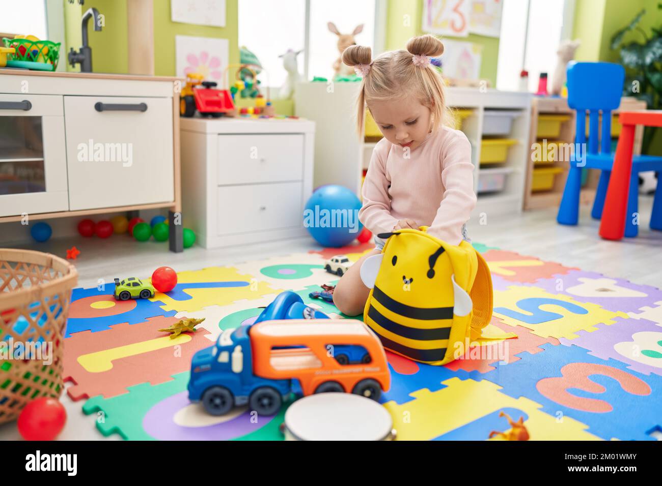 Adorable caucasian girl sitting on floor opening backpack at ...