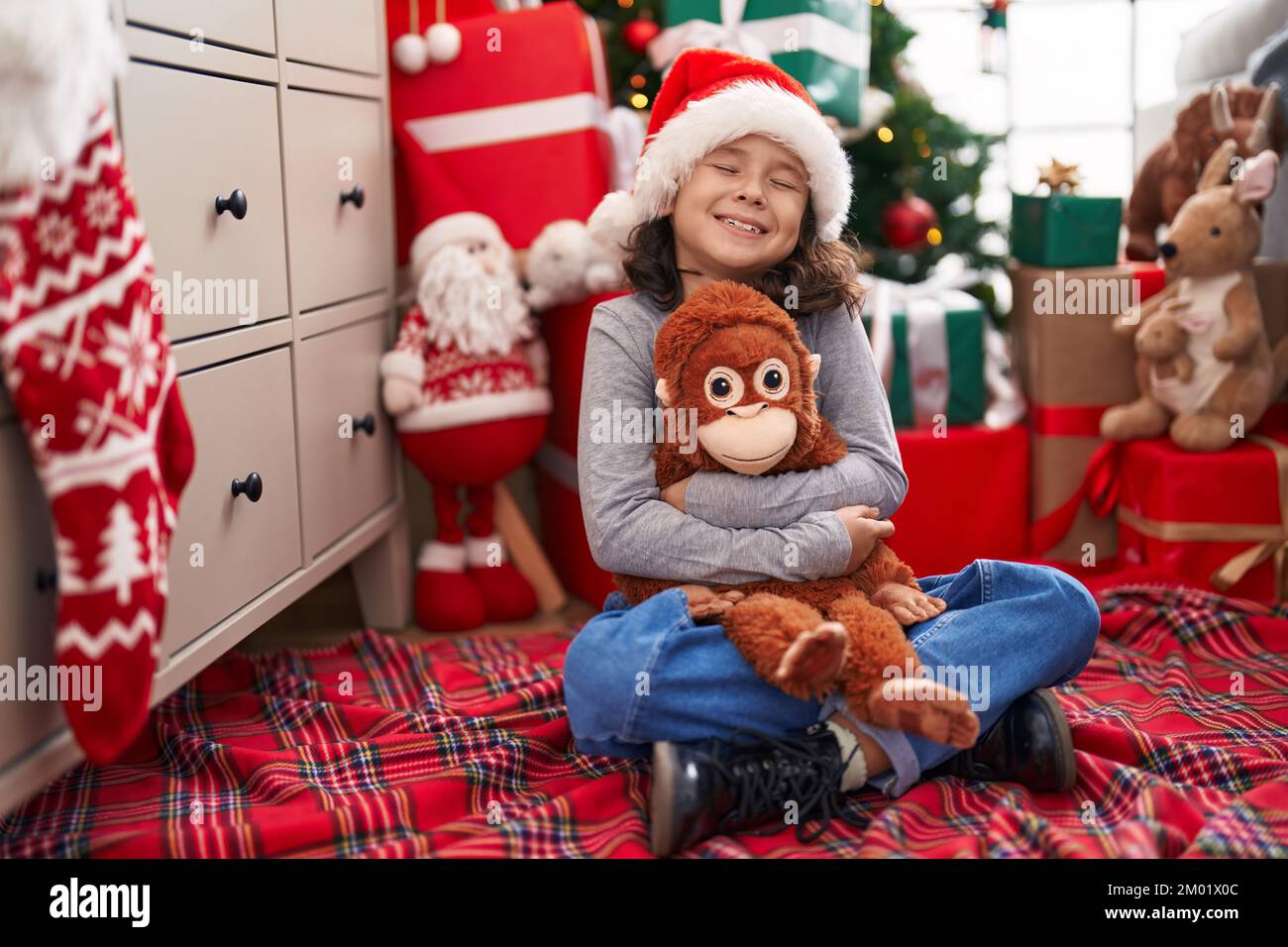 Adorable chinese girl hugging monkey doll sitting on floor by christmas ...