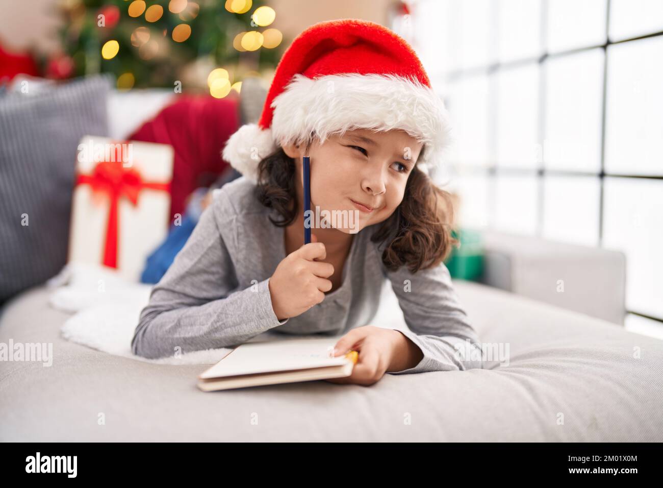 Adorable chinese girl thinking to write lying on sofa by christmas tree ...