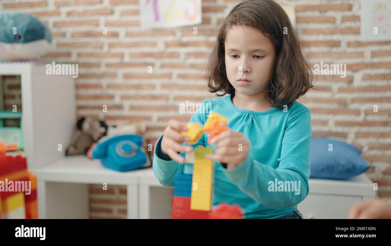 Adorable chinese girl playing with construction blocks sitting on table ...
