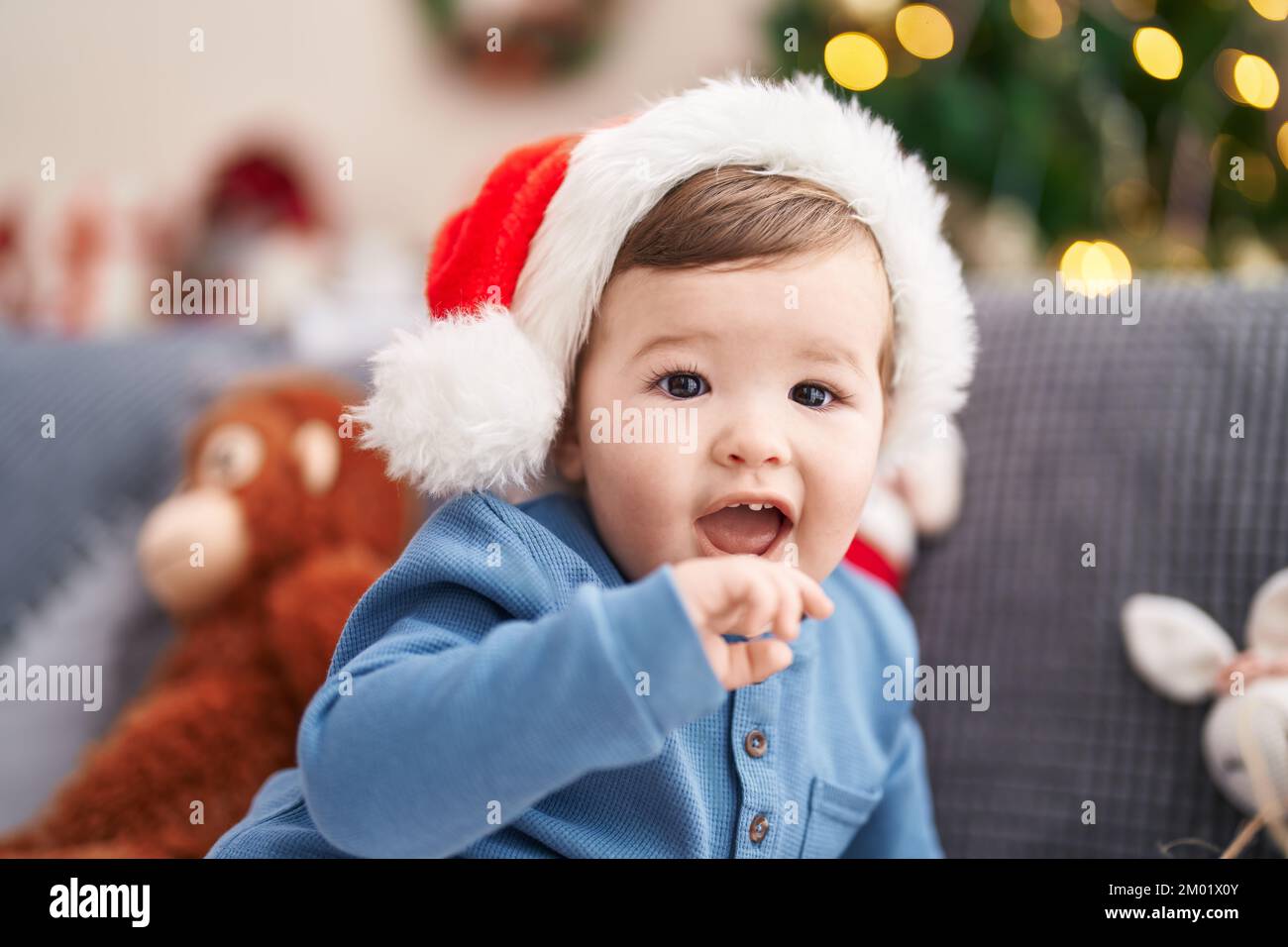 Adorable caucasian baby sitting on sofa by christmas tree with relaxed ...