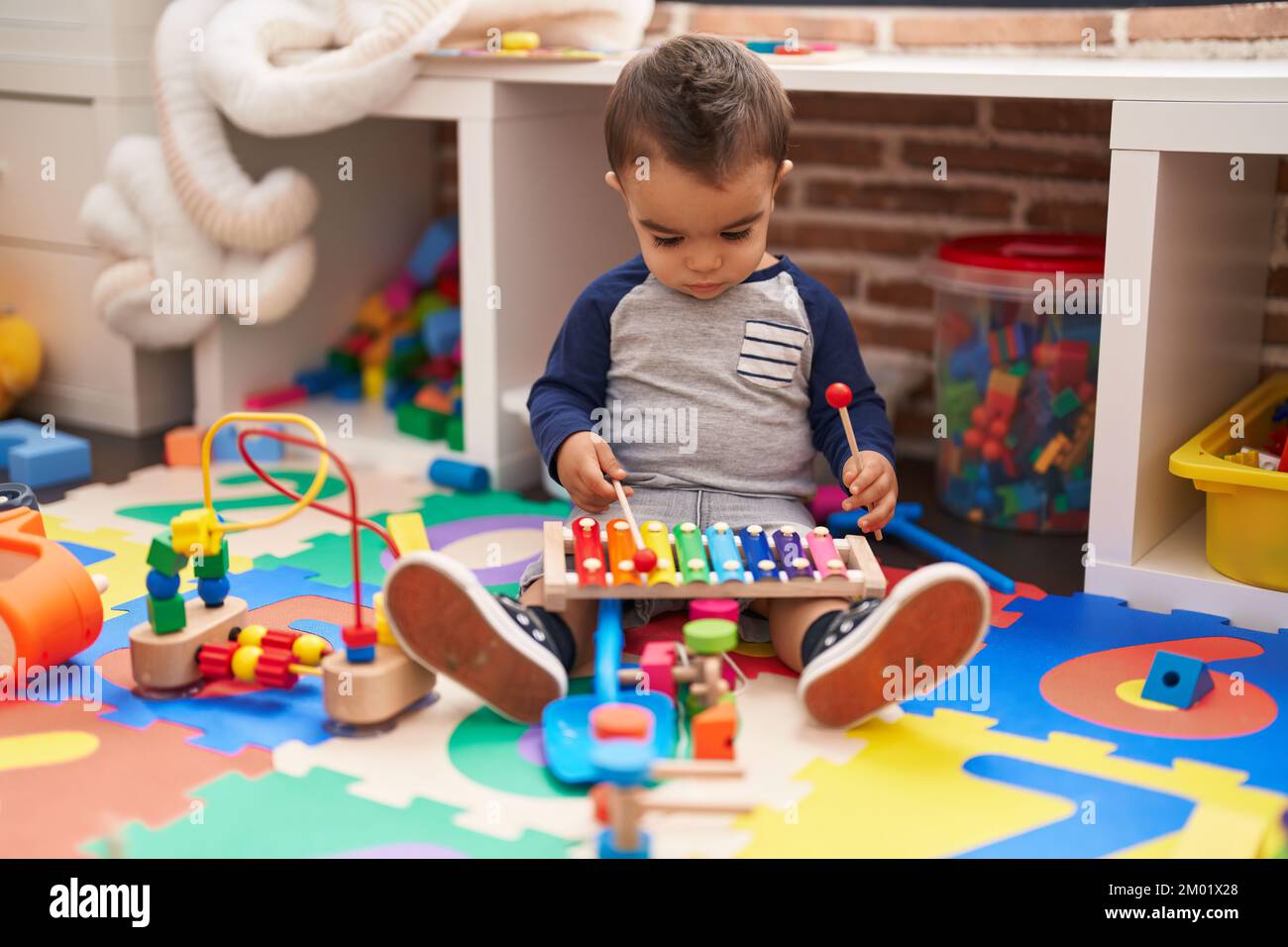 Adorable hispanic toddler playing xylophone sitting on floor at ...