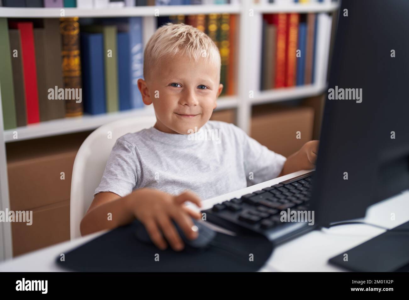 Adorable toddler student using computer sitting on table at classroom ...