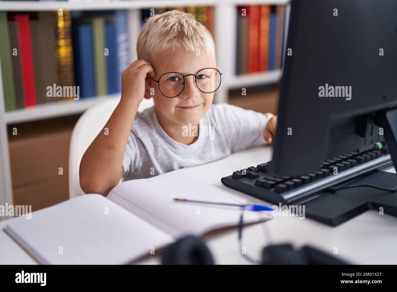 Adorable toddler student using computer sitting on table at classroom ...
