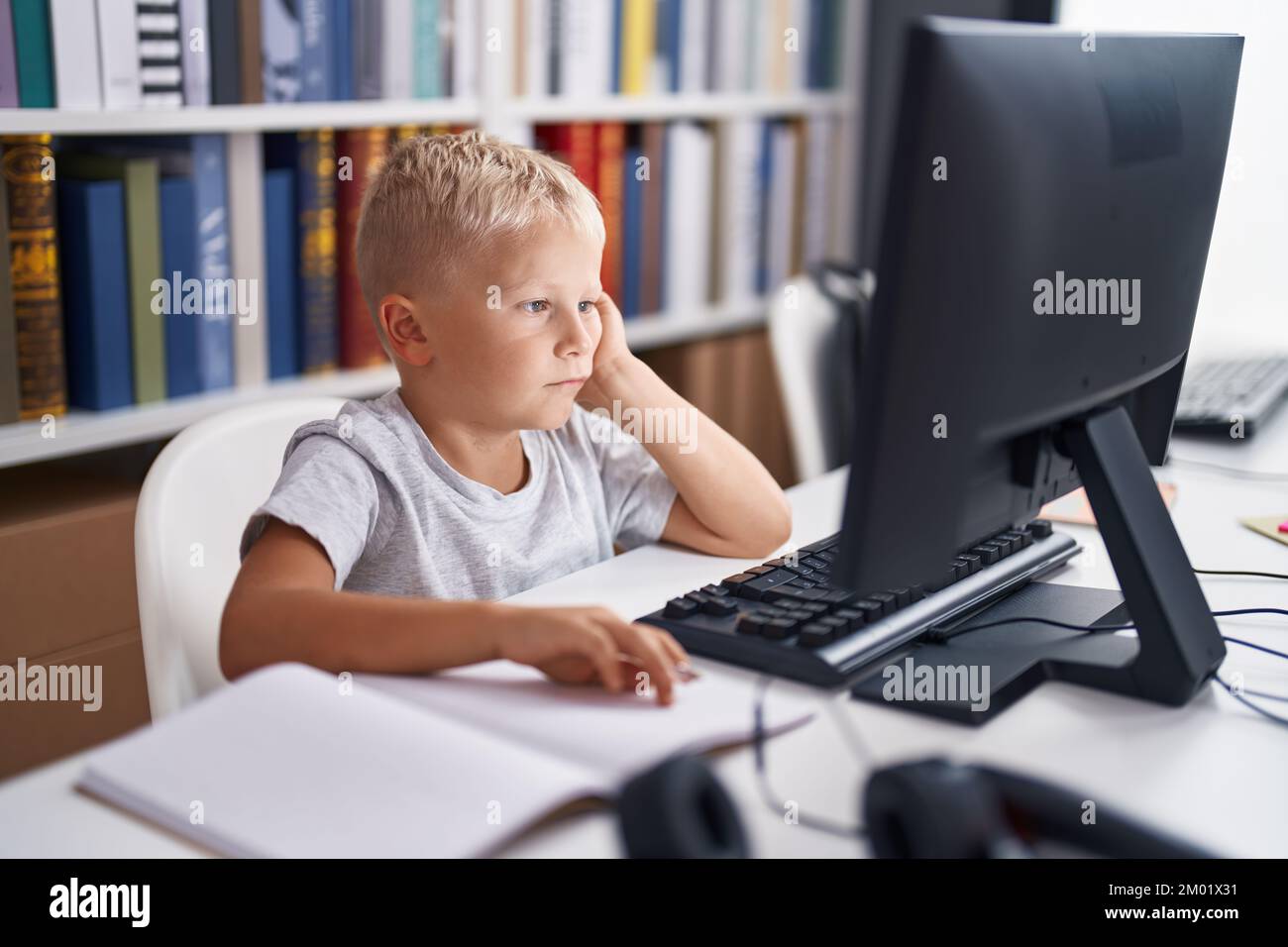 Adorable toddler student boring using computer sitting on table at ...