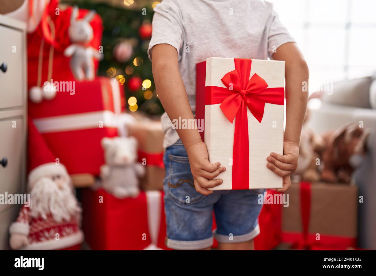 Adorable toddler holding gift standing by christmas tree at home Stock ...
