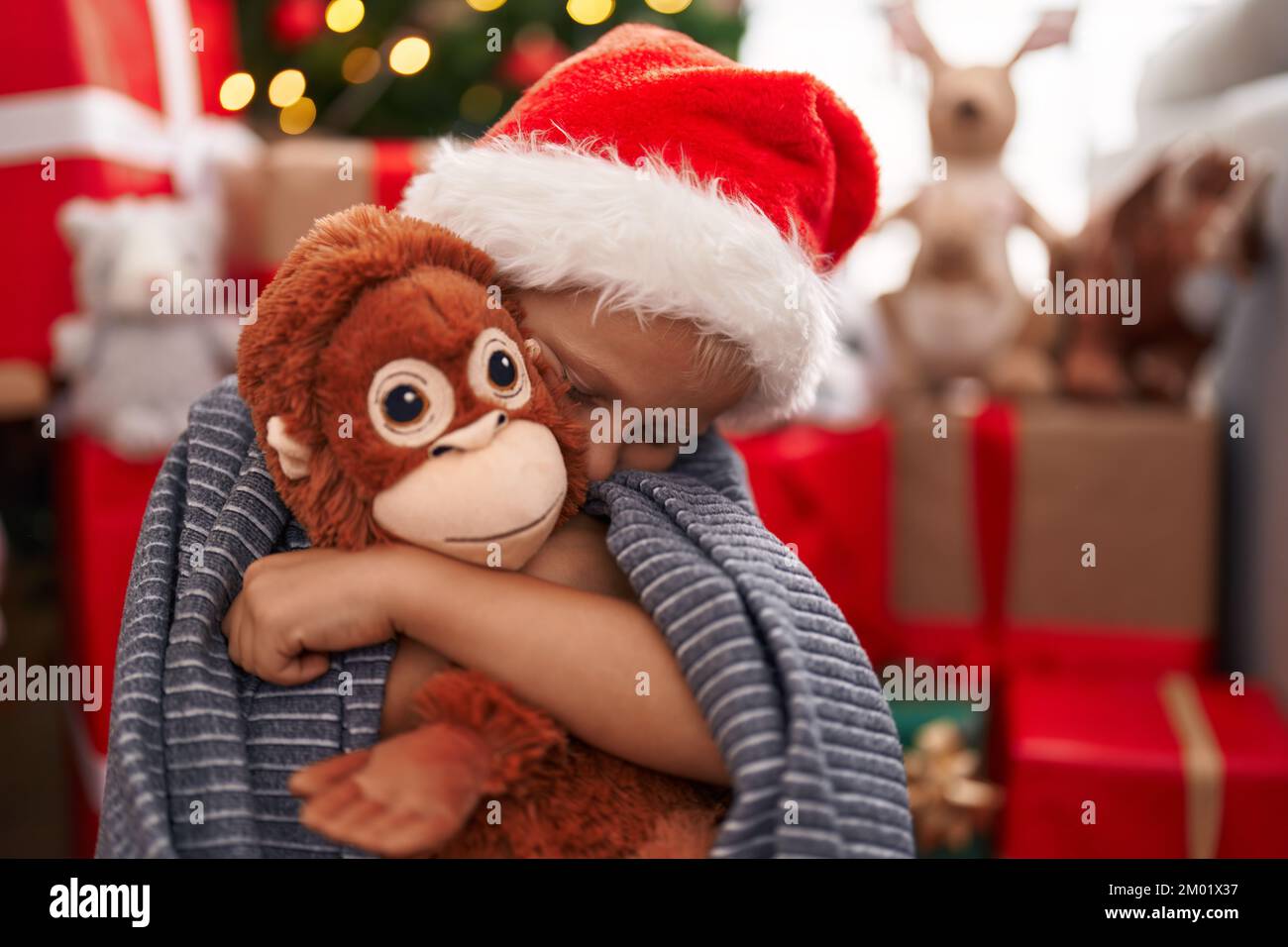 Adorable toddler hugging teddy bear standing by christmas tree at home ...