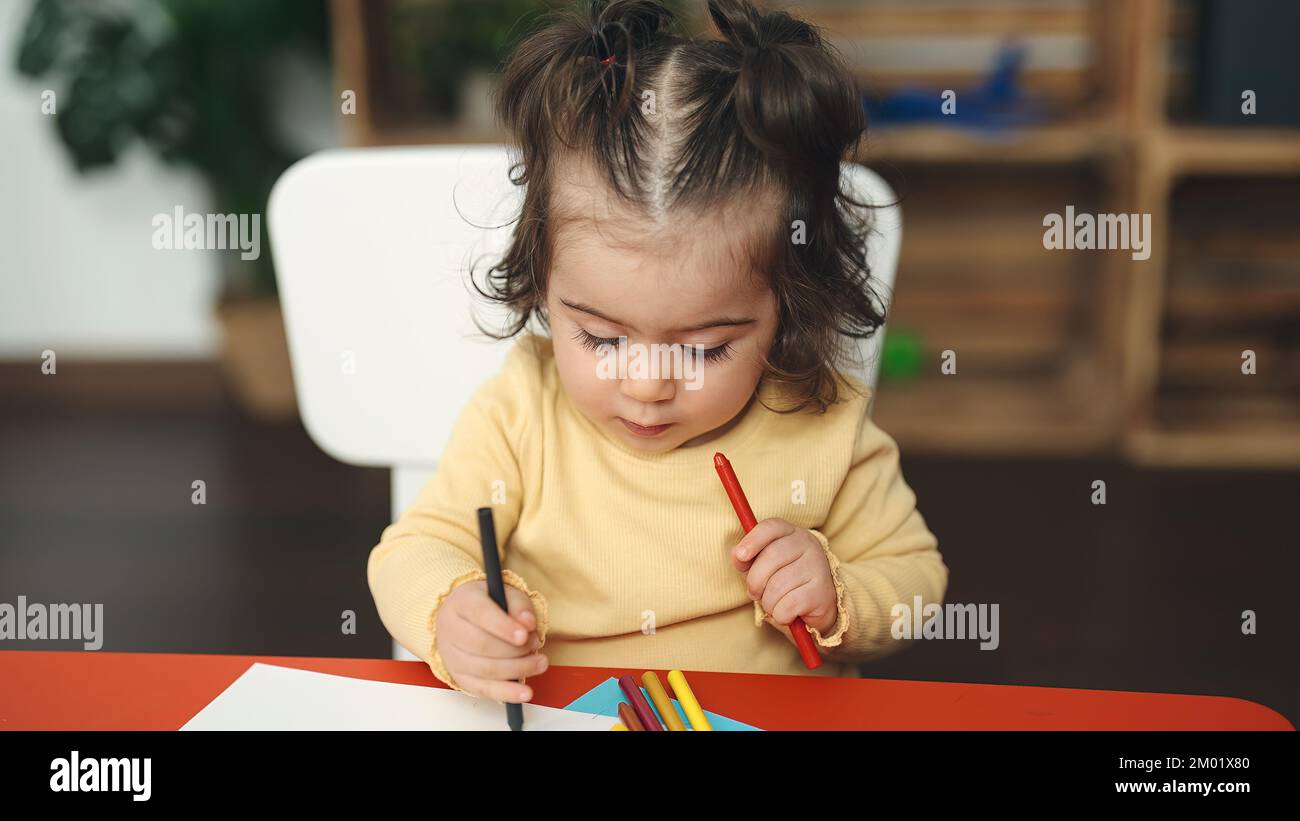 Adorable hispanic girl student sitting on table drawing on paper at ...