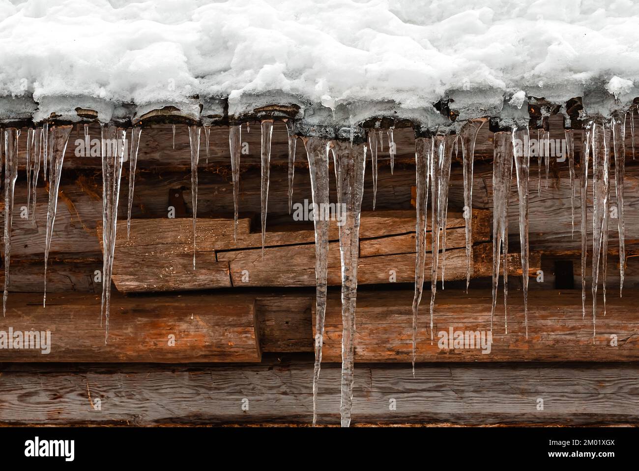 Icicles hang from the snow-covered roof of an old wooden house Stock ...