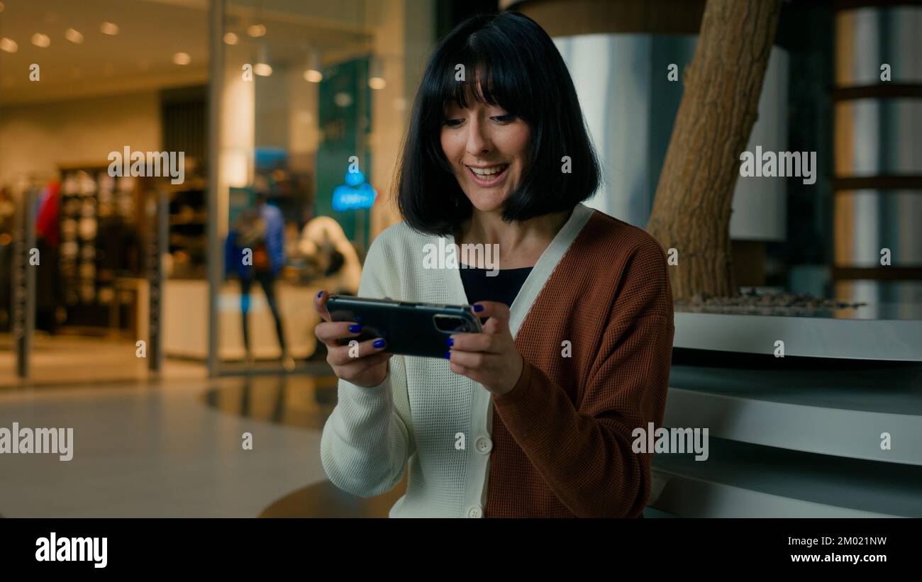 Woman lady female gamer girl indoors in shopping mall sitting playing ...