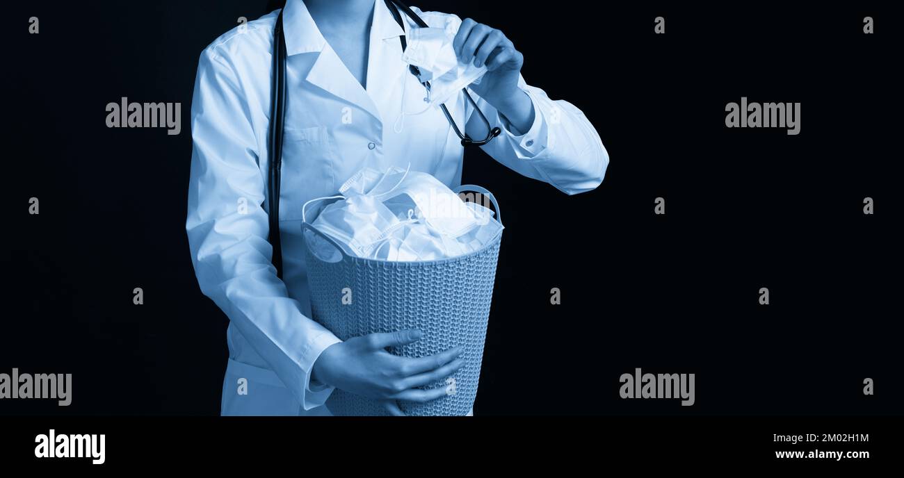Doctor holding bucket full of used facial masks, throwing them away as ...