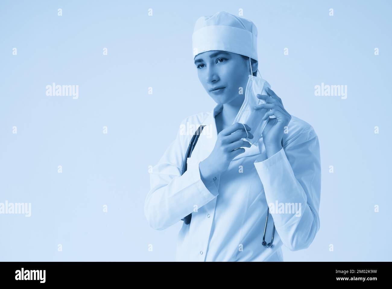 Portrait of young female doctor putting on protective medical face mask ...