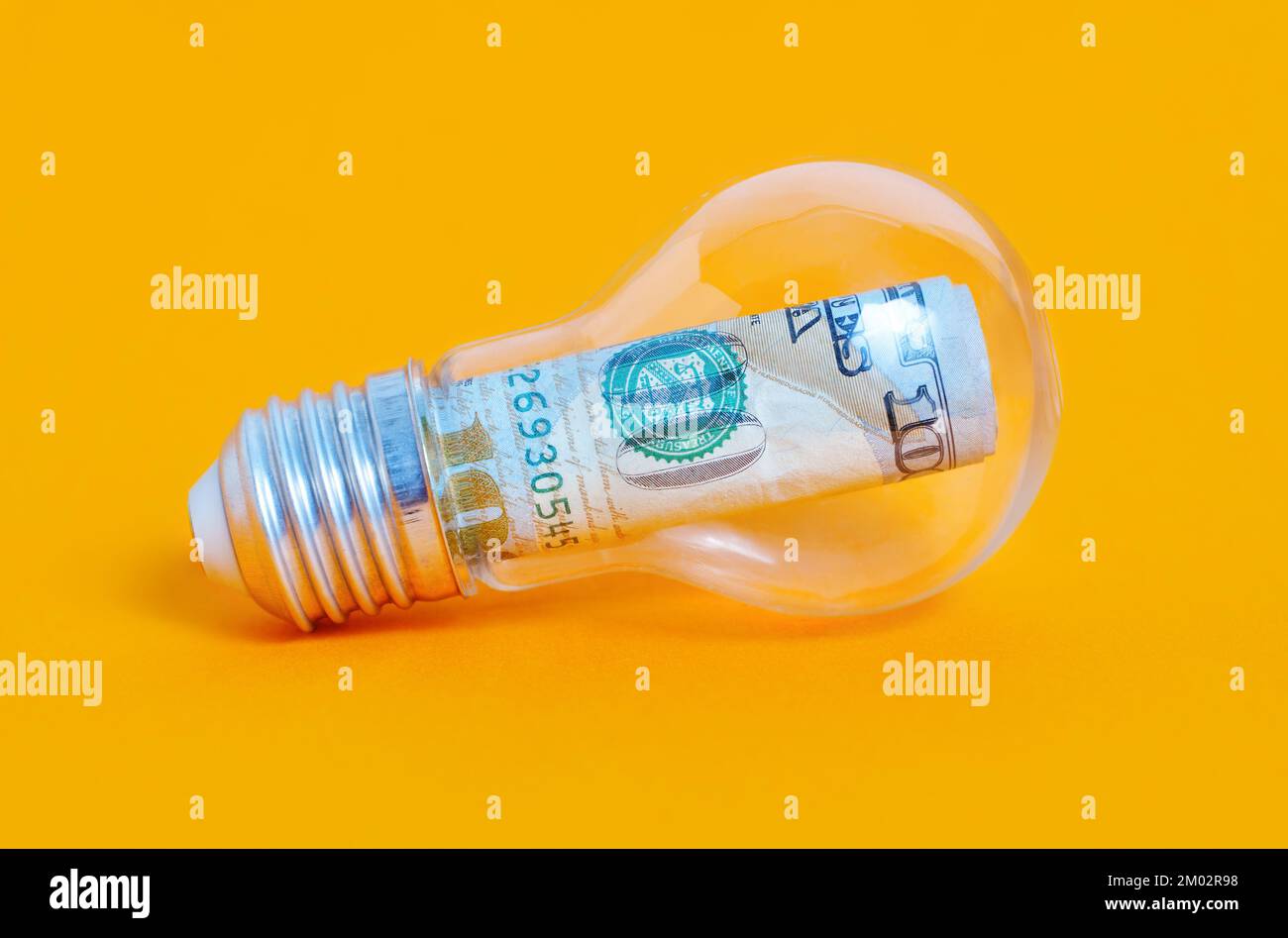 One hundred dollar bill rolled inside a light bulb isolated on yellow ...