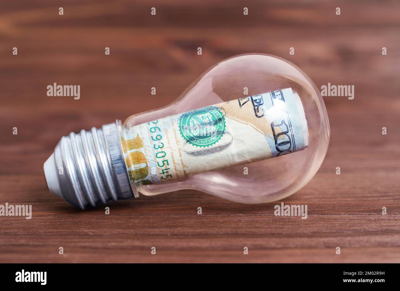 One hundred dollar bill rolled inside a light bulb isolated on a wooden ...
