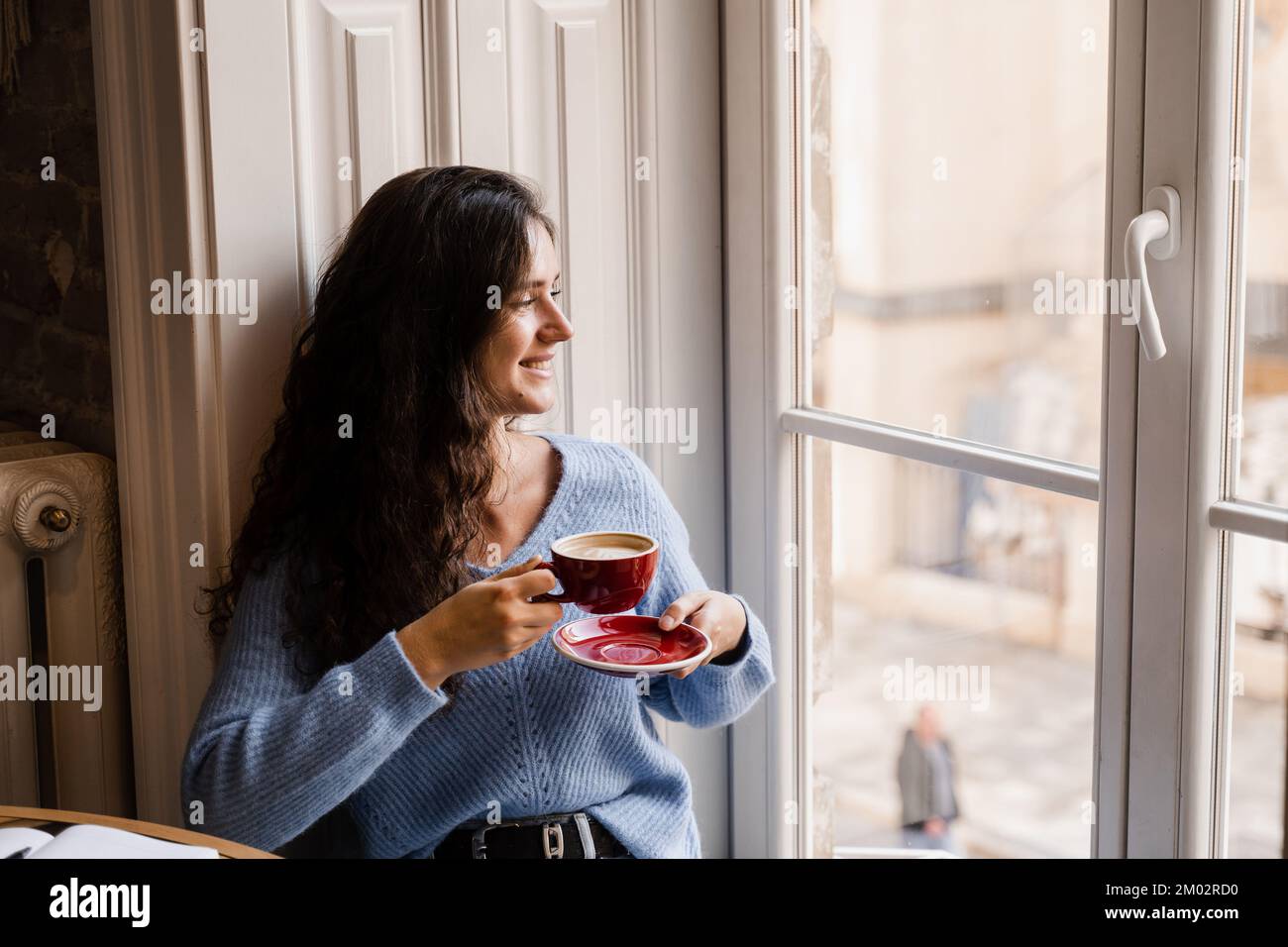 Attractive girl with cup of coffee in cafe with big window. Cheerful ...
