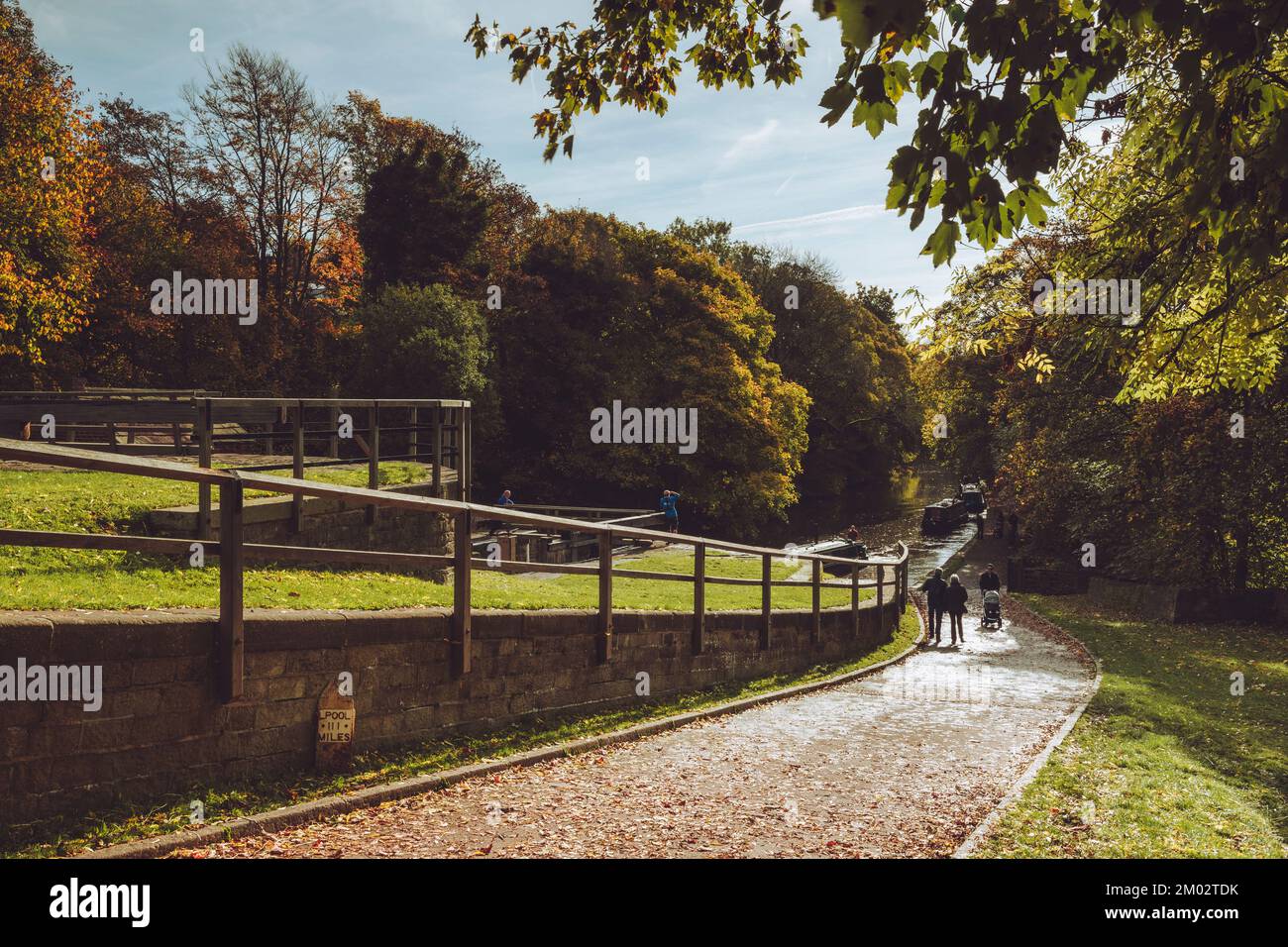 People walking on canal-side path in autumn by lock, boats traveling ...