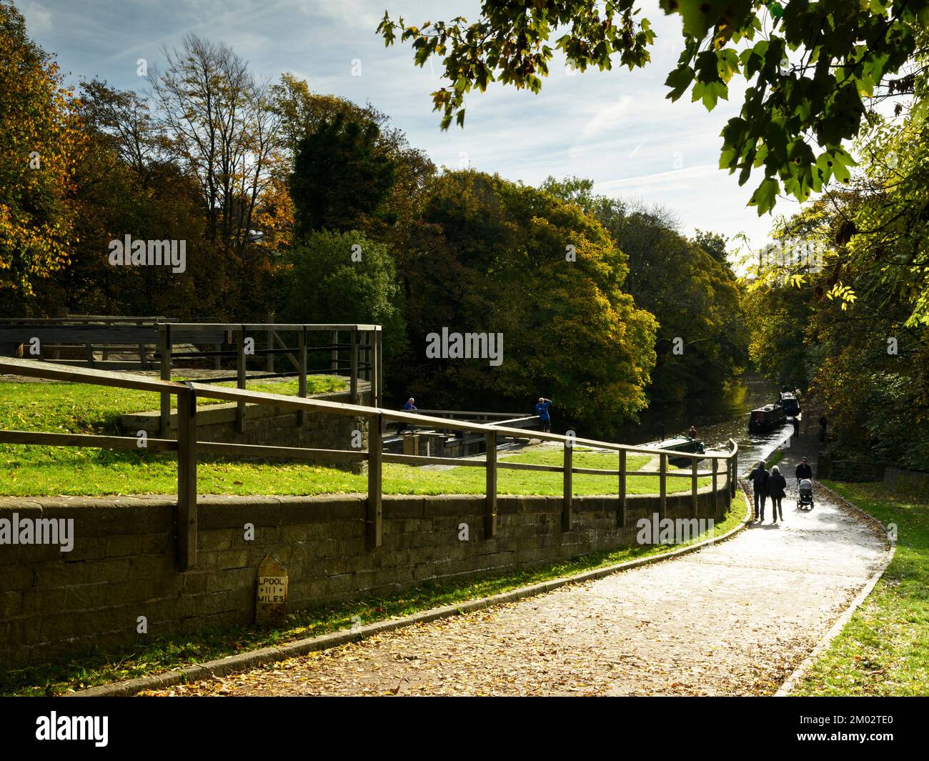 People walking on canal-side path in autumn by lock, boats traveling ...