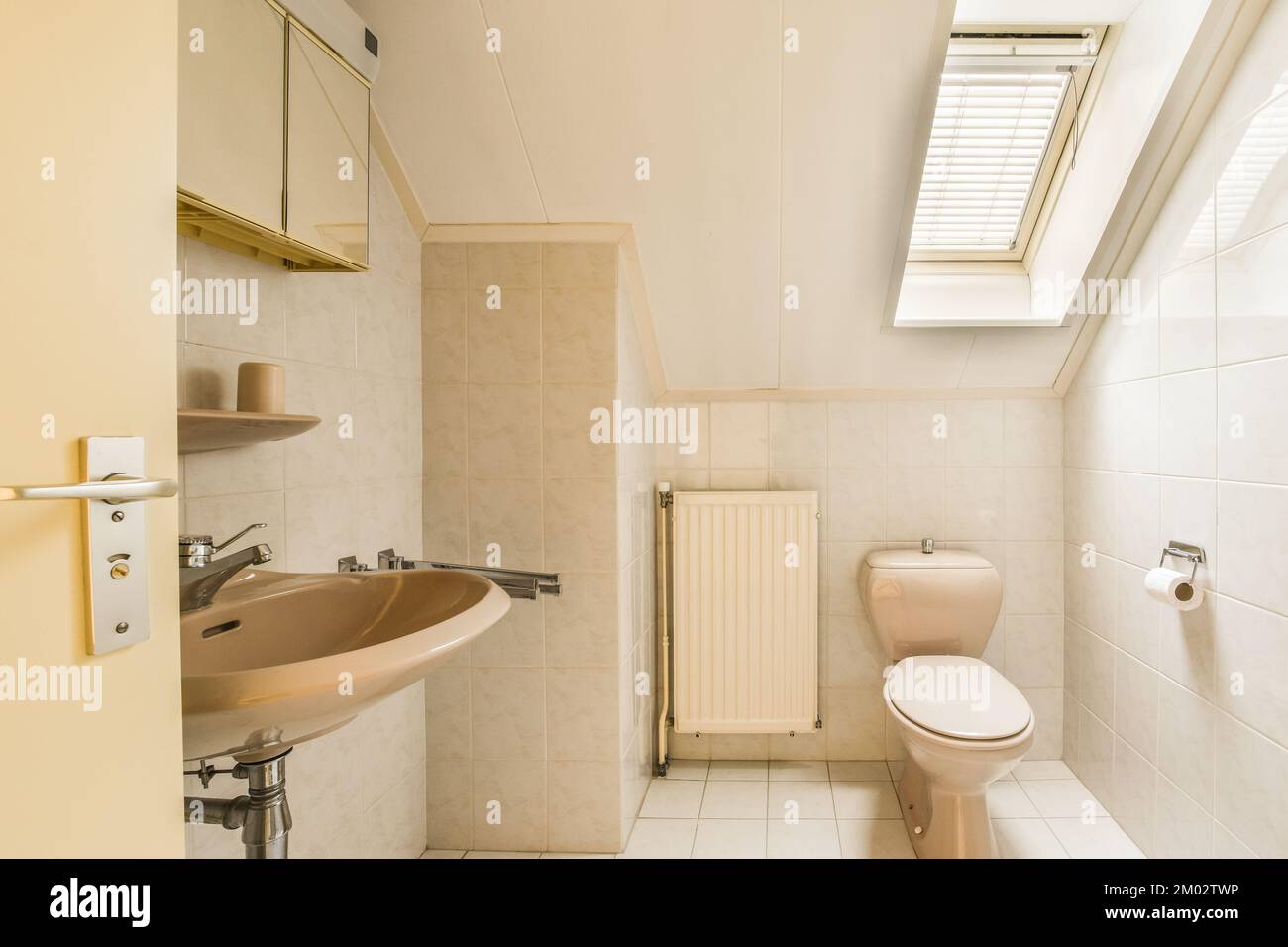 Flush toilet and small sink in corner in lavatory room with beige tile ...