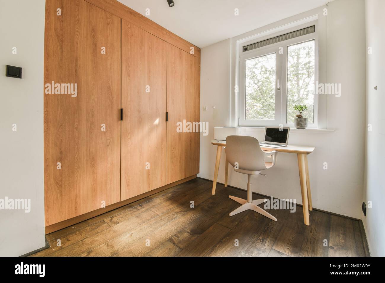 Interior of light home office with wooden desk and wardrobe near window ...