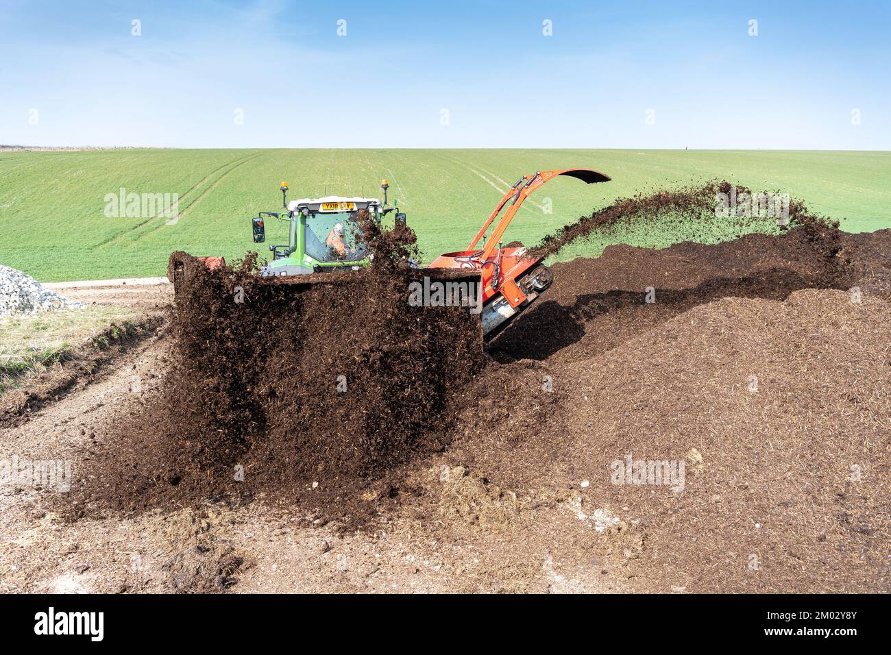 Turning a manure heap over to make compost to spread on farmland, which ...
