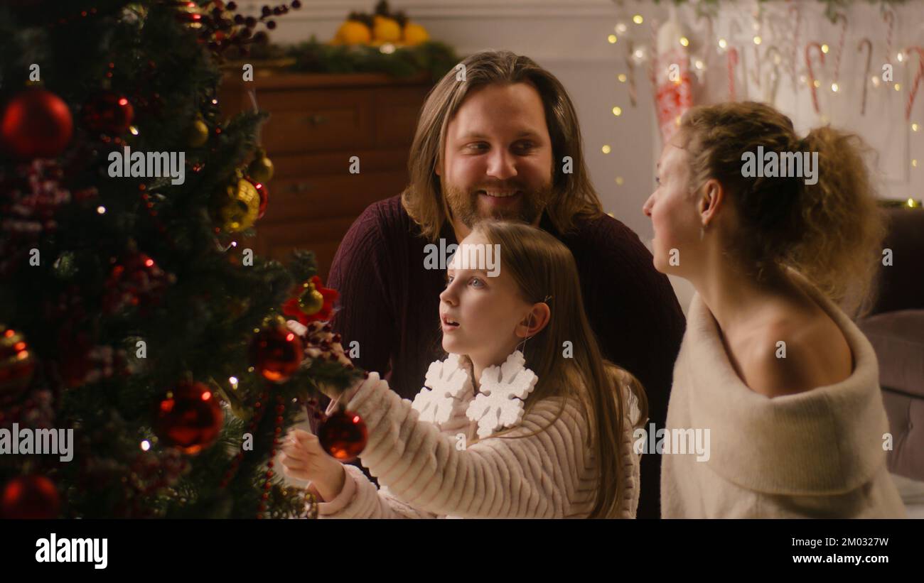 Family sitting together in living room and decorating Christmas tree with branches. Flashing ...